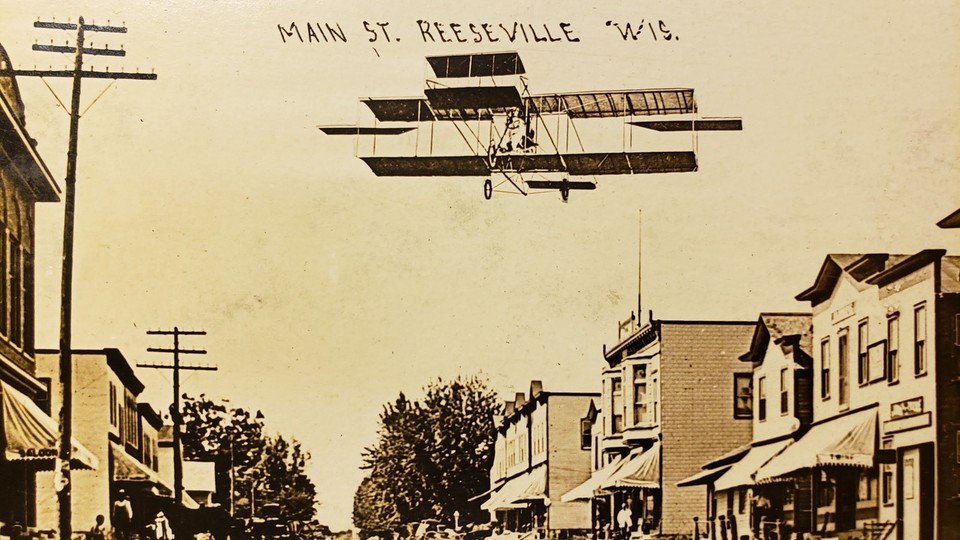1913 RPPC REESEVILLE, WI EARLY BIPLANE FLYING OVER MAIN STREET ...