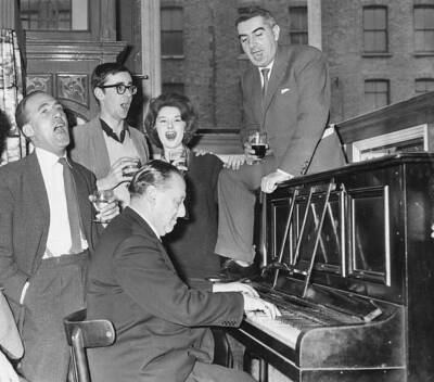 Irish comic actor Milo O'Shea plays piano as cast mates including Pa ...