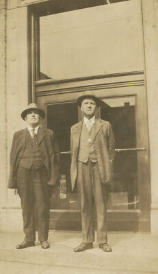 TWO MEN UNCOMFORTABLY POSED, STIFFLY STAND ON SIDEWALK, HUGE WINDOW ...